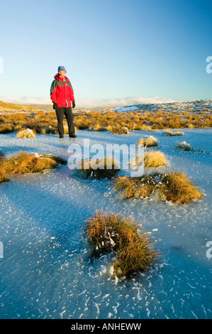 A walker on a frozen tarn on the summit of Red Screes in the Lake ...