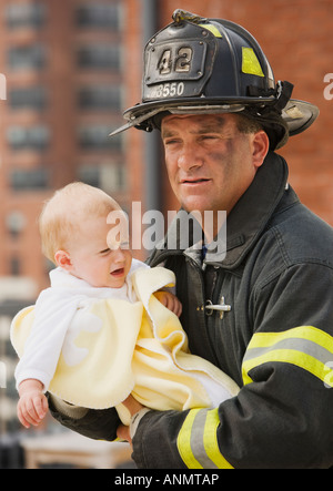 Firefighter hero carrying baby girl out from burning building area from fire incident. Rescue ...