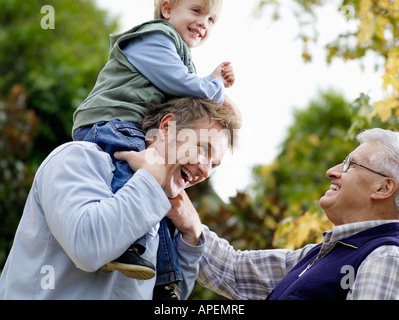 A small boy with father and grandfather sitting in apple orchard in ...