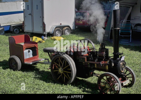 A miniature steam traction engine and trailer being driven at the ...