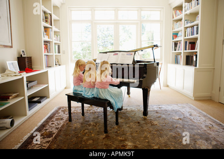 Triplets playing piano in living room (rear view Stock Photo - Alamy