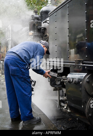 A train engineer in blue overalls crouching down and applying motor oil ...