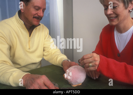 Mature woman putting coin in piggy bank on blue background Stock Photo ...