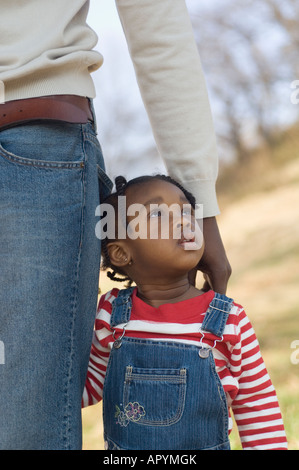 Low view of a toddler standing next to her mothers legs and wanting to ...