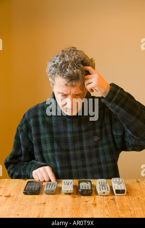 A man confused over which remote control to pick Stock Photo - Alamy