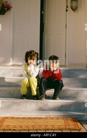 Two children, a boy and a girl, patiently sit in an airport terminal ...