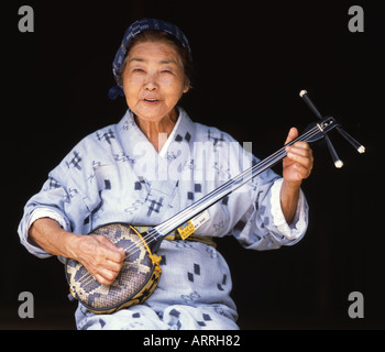 A woman plays the sanshin, traditional Okinawan instrument, in front of ...
