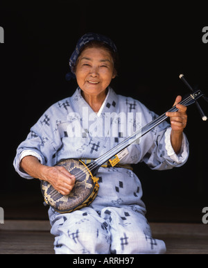 A woman plays the sanshin, traditional Okinawan instrument, in front of ...
