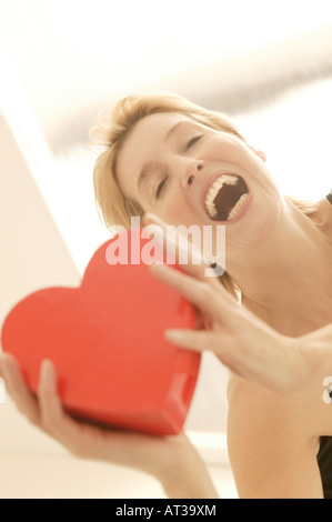 smiling woman hold heart present box on blue background Stock Photo - Alamy