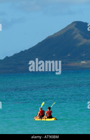 Two people in a kayak paddling on calm blue water, with cliffs in the ...