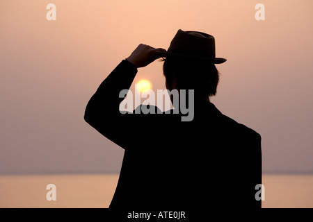 Asian man silhouette looking at sunset under a palm tree on the beach ...