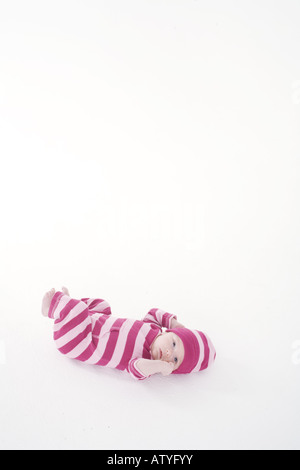 A little girl curled up and laying on a white background in the studio ...