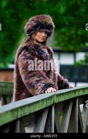 Woman wearing fake fur coat and enjoying walk outdoors in winter park ...