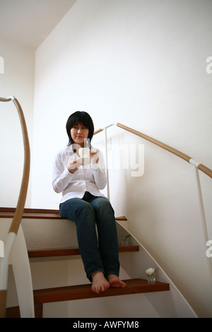 Young woman with cup of coffee sitting at table in office Stock Photo ...