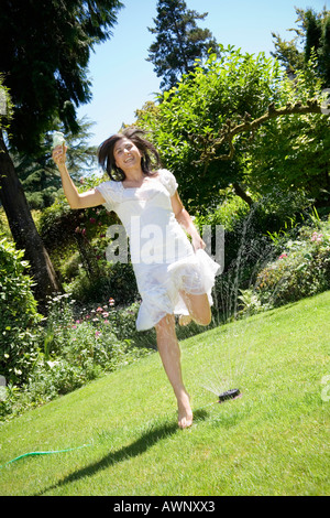 A young woman running through a sprinkler in the grass Stock Photo - Alamy
