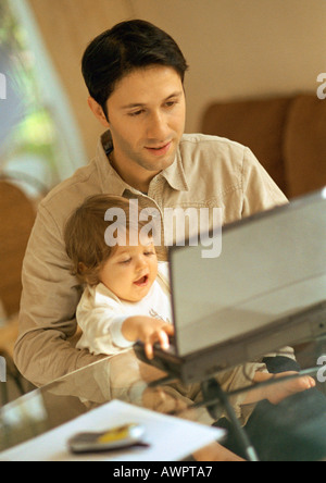 Father multi-tasking using computer laptop at home. Candid authentic ...