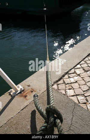 A nautical rope with a single knot, tied loosely to a wooden piling to ...