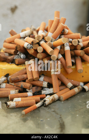 An overflowing yellow ashtray on a table Stock Photo - Alamy