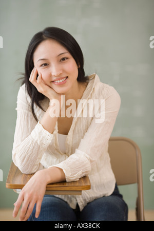 Young Asian woman sitting at desk writing notes on tablet smiling ...