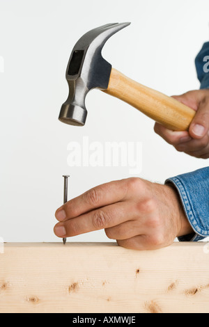 Male hand hold hammer and nail a clothespin, wooden work bench table ...