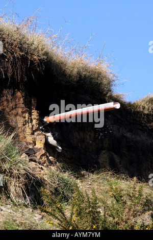 A ONCE BURIED PIPE EXTENDS FROM THE ERODED CLIFF FACE AT DUNWICH ...