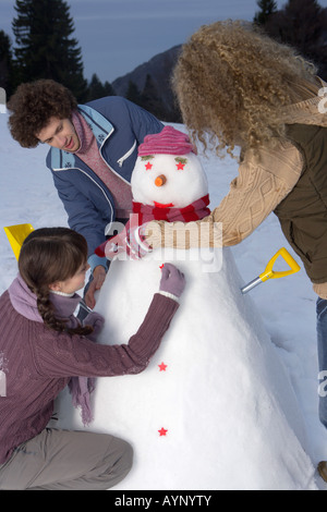Group of friends building a snowman outdoors during winter, enjoying ...
