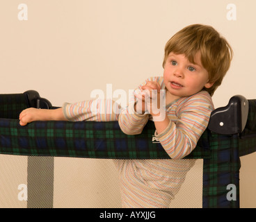 two year old boy climbing out of cot, escaping travel cot, bed, pen ...