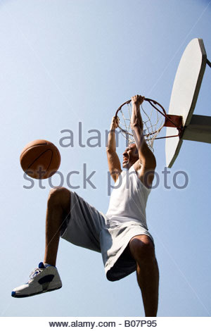 A basketball player hanging from the rim after slam dunking the ball ...