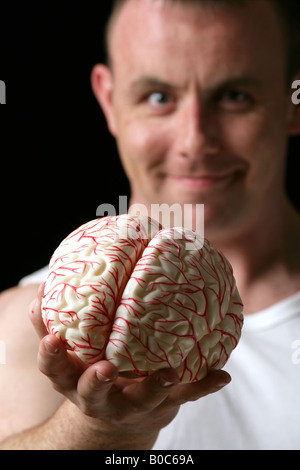 Hand holding a model of a brain on top of a green paper cut-out of a ...