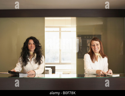 Smiling receptionist behind the hotel counter attending female guest ...
