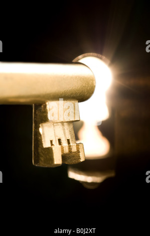 A golden key in a keyhole illuminated by a mysterious light coming from ...