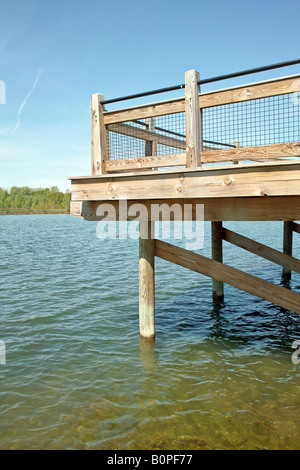 A small wooden dock on the lake surrounded by hills covered in greenery ...