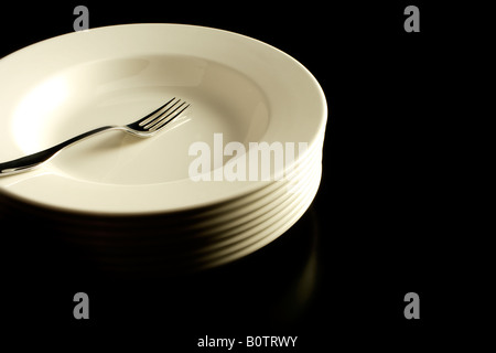 Plates with fork against black background Stock Photo - Alamy