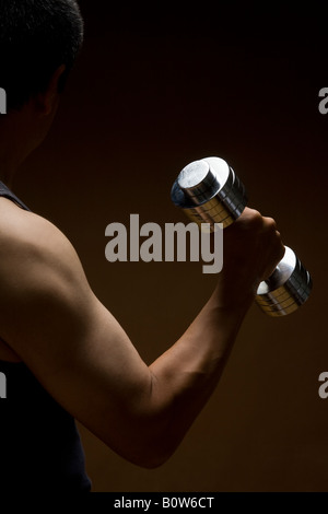Midsection side view of muscular man lifting dumbbell against black ...
