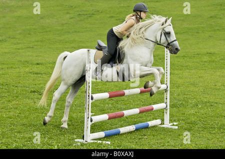 Young girl jumping a white horse pony over a jump at a showjumping ...
