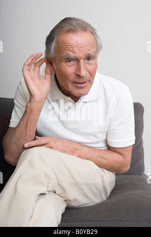 Portrait of a hard of hearing man sitting in a office leather armchair ...