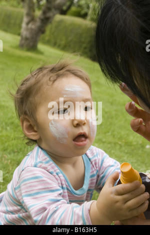 Mother applying sun protection cream on a smiling boy's cheek, enjoying ...