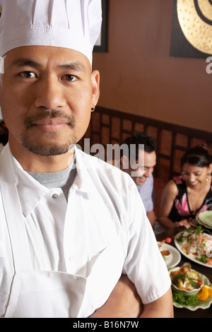 Portrait of mature Asian male chef in uniform presenting an empty plate ...