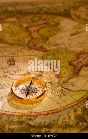 An antique gold compass set upon a sixteenth century map of the world ...