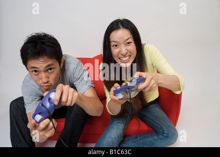 young Asian woman playing video game with controller sitting on sofa at ...