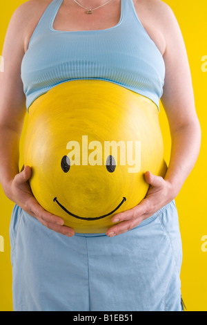 View of pregnant woman's belly with yellow Smiley Face painted on her ...