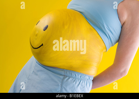 View of pregnant woman's belly with yellow Smiley Face painted on her ...
