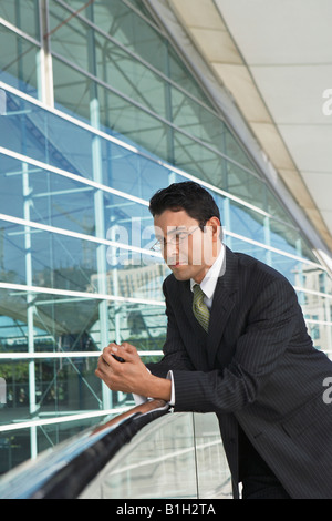 Businessman leaning on railing outside office building Stock Photo - Alamy