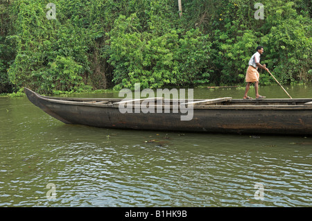 Indian man using a pole to propel canoe with another man and woman ...