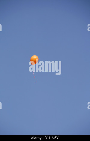 one orange balloon floating up in blue sky Stock Photo - Alamy