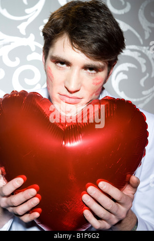 young man holding angry balloon in front of face, isolated on yellow ...