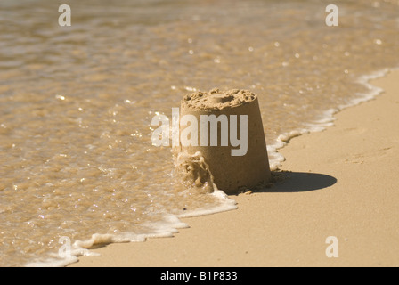A child's sand castle about to be washed away by the incoming tide ...