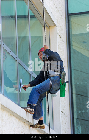 One office Window cleaner suspended high up in a seat harness on an ...