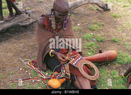 Maasai married woman with shaved head making traditional bead necklace ...
