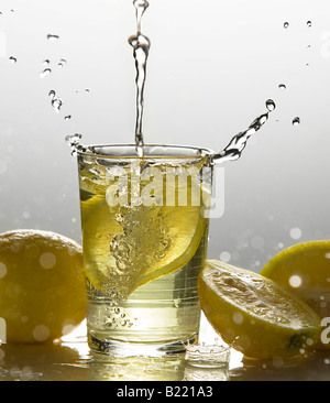 Vertical shot of lemon slices splashing into glass water on isolated ...